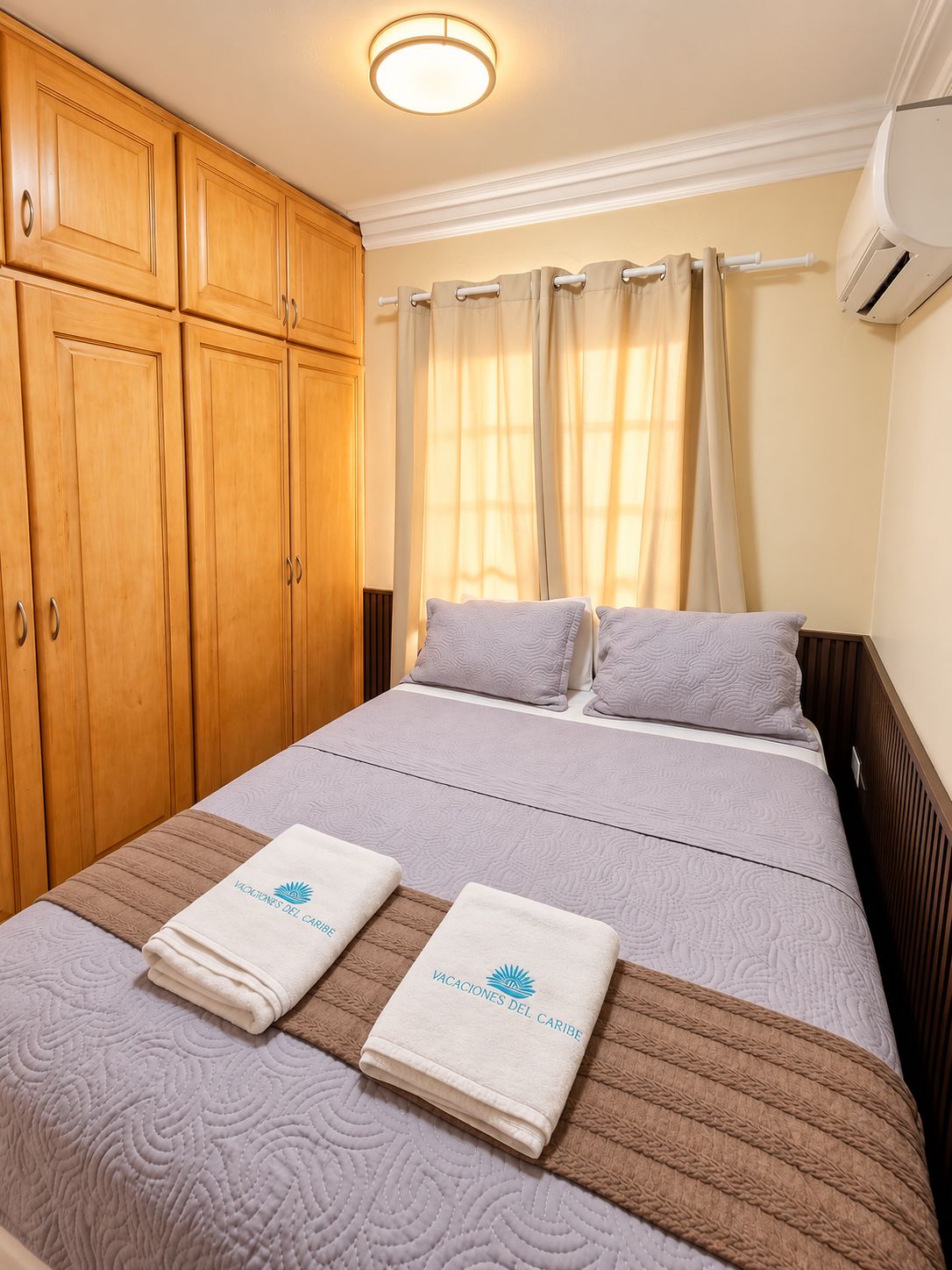 Quarto de hotel com cama grande, guarda-roupa de madeira e luminária no teto.