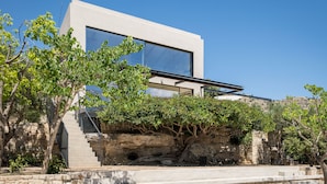 Um edifício moderno com uma ampla janela de vidro, escadas e vegetaç ão ao redor.