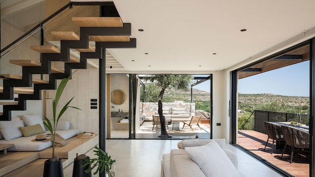 Um interior moderno com uma escada, uma área de estar com sofá e vista para um pátio externo.