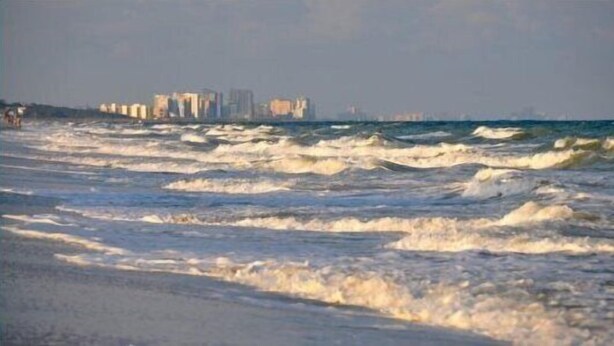 Uma praia com ondas e o horizonte de uma cidade ao longe.