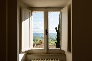 Janela com vista para paisagem rural, incluindo um edifício e árvores.