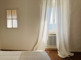 Quarto com uma cama, janela com vitrais e cortinas leves.