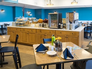 Espaço de buffet de café da manhã com variedade de alimentos, geladeira e estação de café.