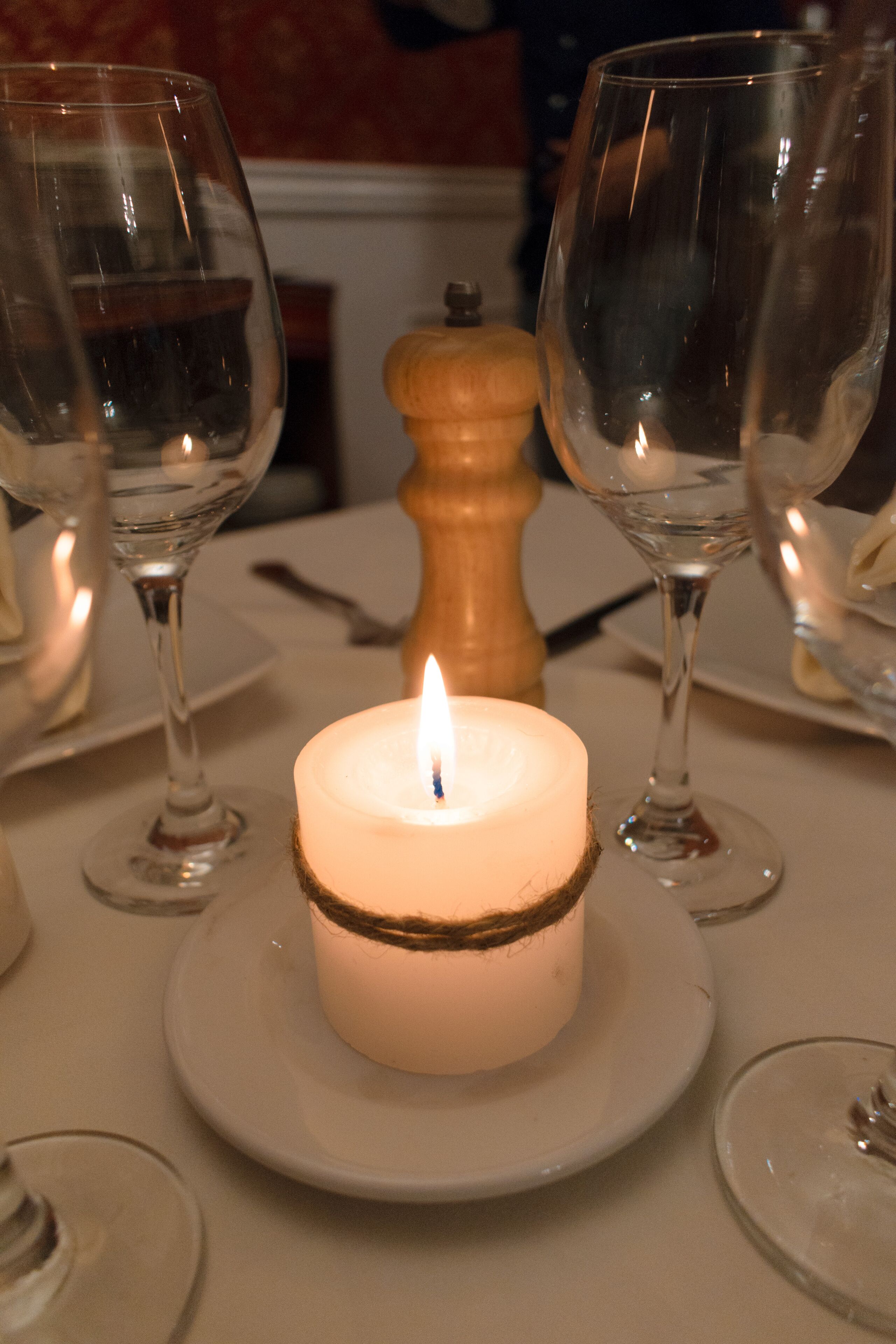 Uma mesa com uma vela acesa, duas taças de vinho e um saleiro.