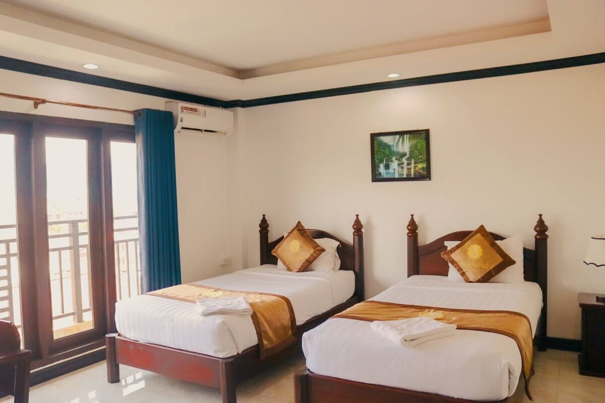 Quarto de hotel com duas camas, uma janela grande com vista e um ar condicionado.
