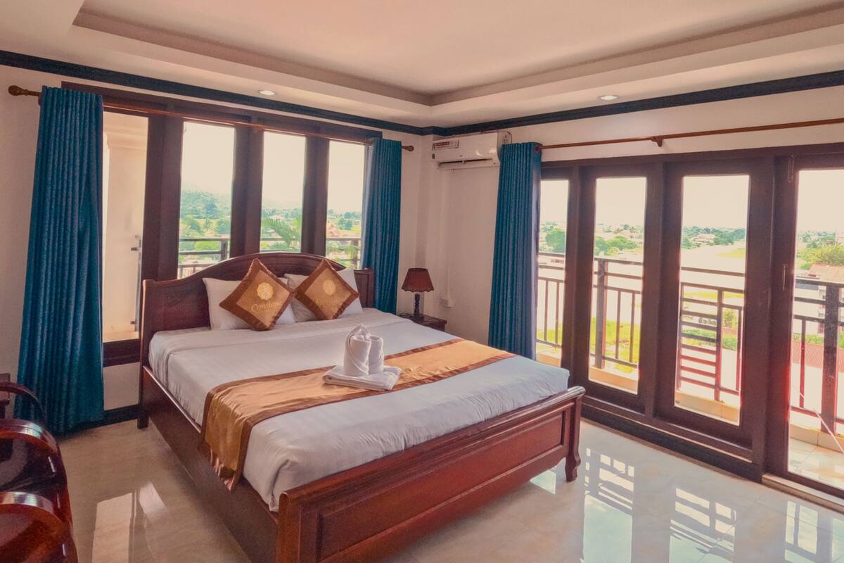 Um quarto espaçoso com uma cama grande, duas janelas e uma varanda.