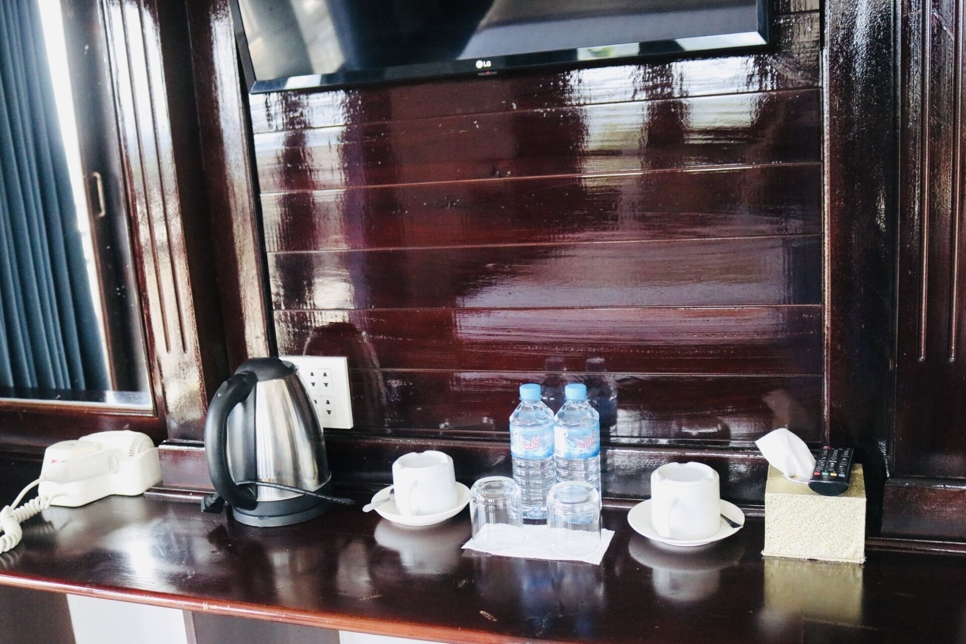 Balcão de quarto de hotel com cafeteira, duas garrafas de água, controle remoto e telefone.