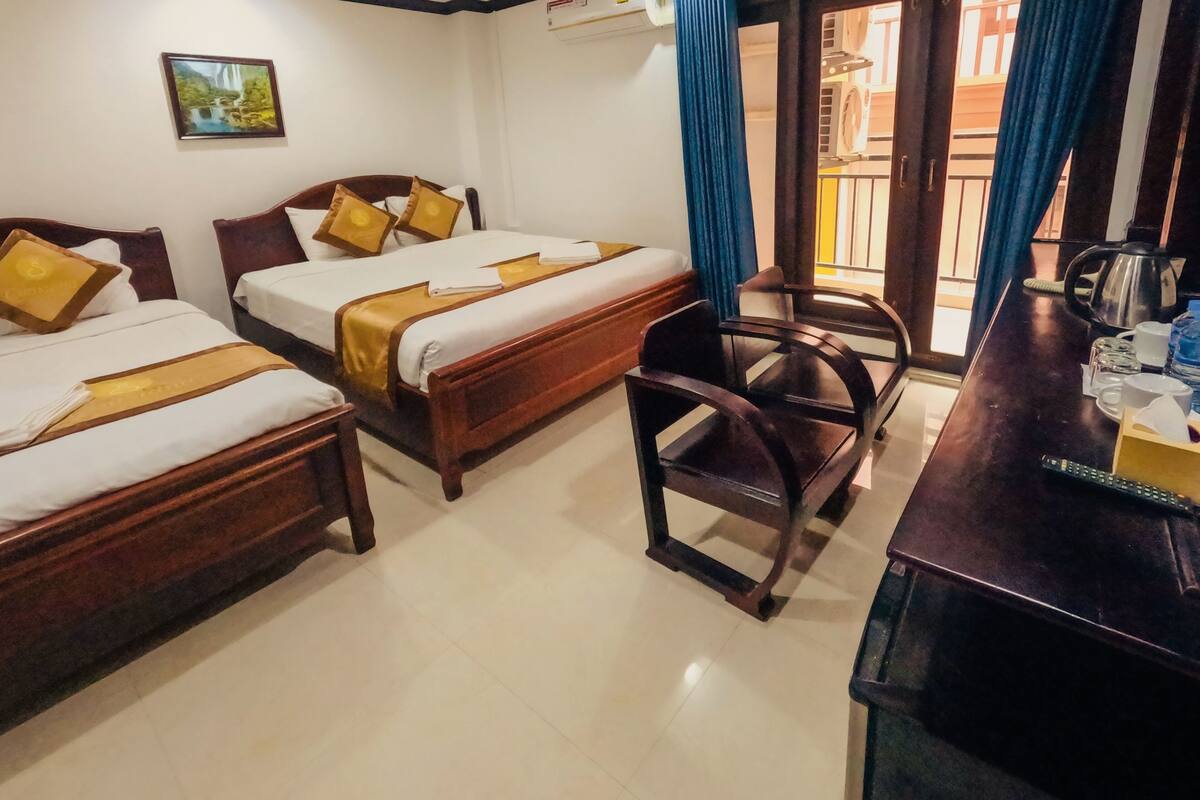 Quarto de hotel com duas camas, uma escrivaninha, uma cadeira e vista para o exterior.