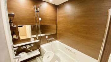 Casa de banho moderna com banheira, sanita e um espelho grande.