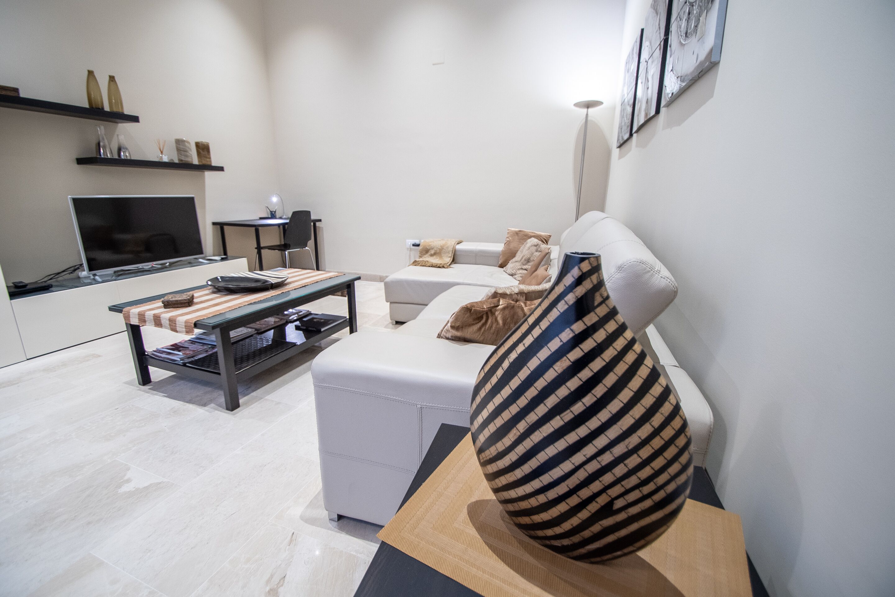 Uma sala de estar moderna com um sofá branco, uma mesa de centro, uma televisão e estantes com objetos decorativos.