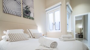 Quarto de hotel com cama, almofadas, toalha enrolada e uma obra de arte na parede.