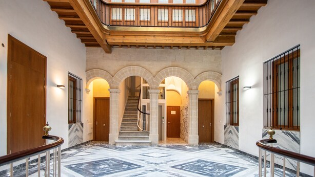 Um hall amplo com piso de mármore, escada e corrimãos de madeira.