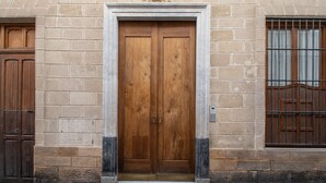 Uma porta dupla de madeira com estrutura metálica, embutida em um edifício de pedra com uma janela com grades de metal.