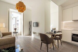 Uma sala de estar moderna com sofá, mesa de jantar com cadeiras, TV na parede e cozinha com armários e fogão.