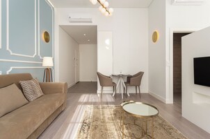 Uma sala de estar moderna com sofá, mesa de centro, área de jantar com cadeiras e TV na parede.