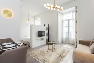 Quarto de hotel moderno com área de refeições, TV, sofá e uma janela grande.