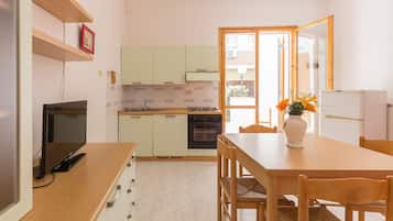 Uma cozinha compacta com área de refeições, uma TV e um vaso com flores na mesa.