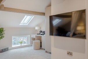 Quarto moderno com claraboia, uma televisão de tela plana grande, uma mesa redonda pequena e janela com vista para o exterior.