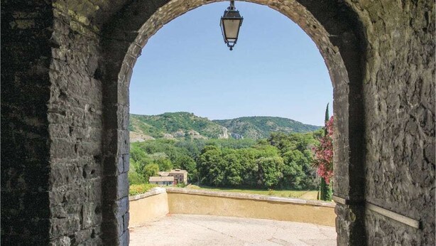 Porta de pedra arqueada que dá para um terraço com vista para colinas verdes e um céu claro.