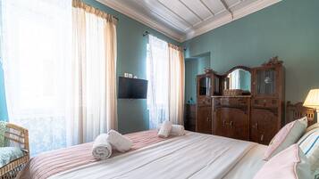 Quarto com cama, cortinas, penteadeira, televisão e abajur.