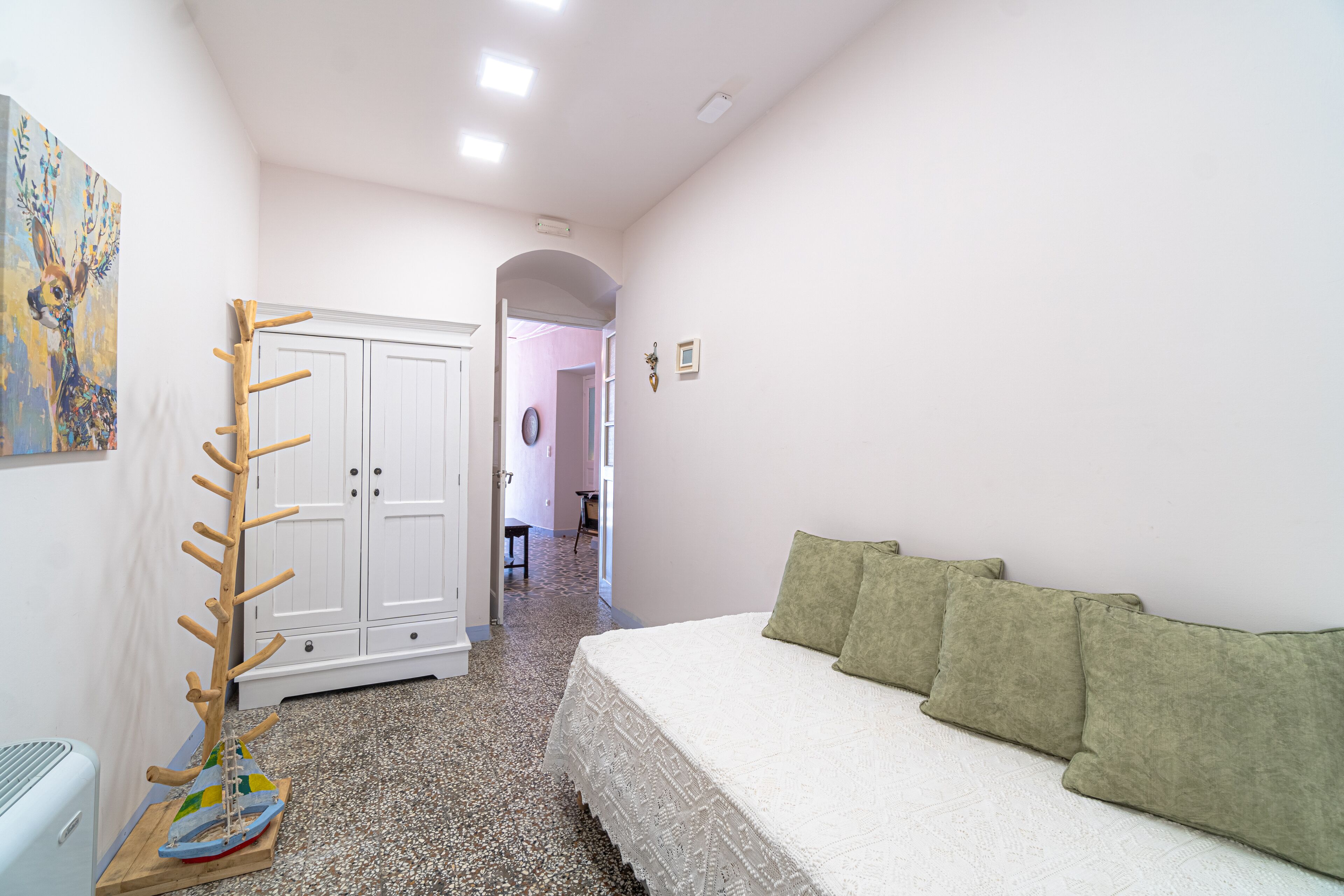 Quarto com cama, um cabideiro de madeira, guarda-roupa e um quadro na parede.
