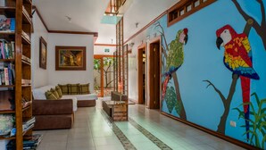 Um hall de hotel com um sofá, estantes de livros, uma mesa de centro e um mural colorido de araras.