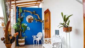 Quarto com parede azul decorativa, mobiliário branco trabalhado e diversas plantas em vasos.