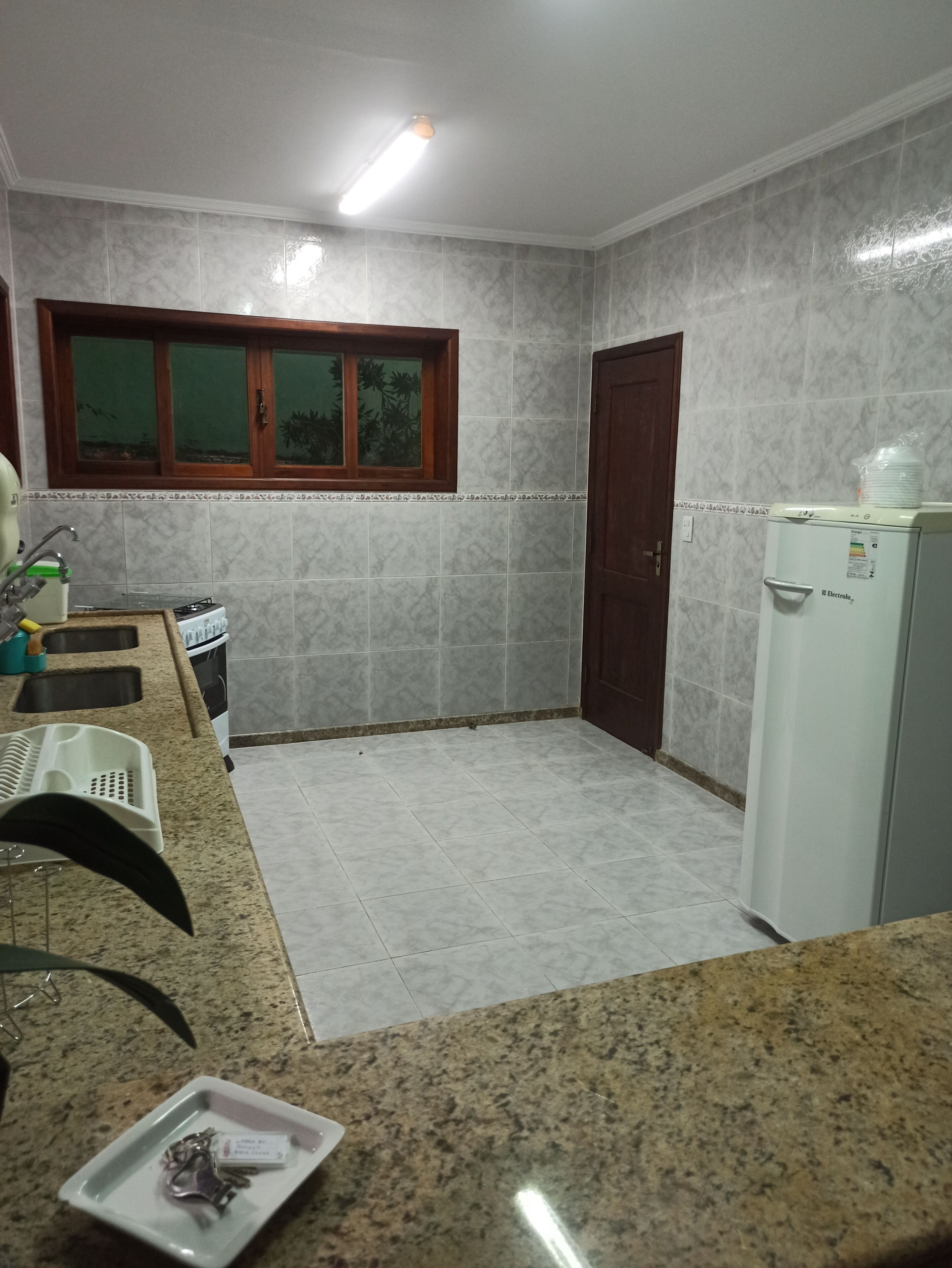 Uma cozinha compacta com bancada de granito, pia embutida, janela com moldura de madeira e geladeira branca.