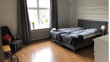 Quarto com duas camas, uma cadeira, radiador e janela com cortinas.