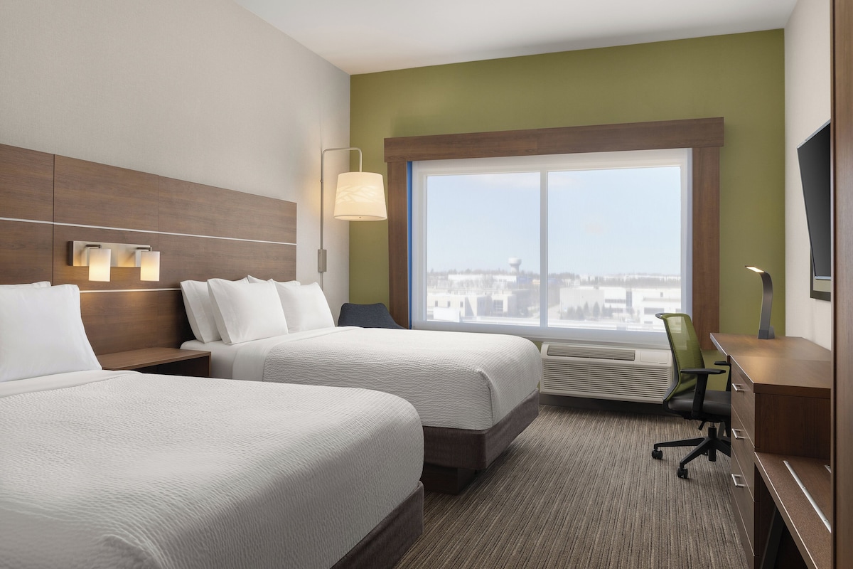 Quarto de hotel com duas camas, uma escrivaninha, uma cadeira, uma janela grande com vista e uma televisão de tela plana.