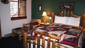 Um quarto rústico com cama de madeira, colcha, abajur e um letreiro com a inscrição "ELK RUN RANCH".