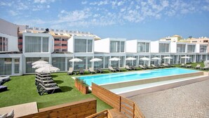 Uma área de piscina no terraço com espreguiçadeiras e guarda-sóis, cercada por edifícios modernos com grandes janelas.