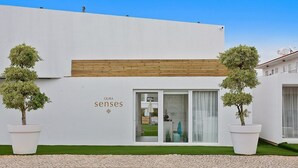 Um edifício moderno com fachada branca, design de ripas de madeira sobre a entrada e duas árvores em vasos de cada lado.
