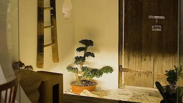 Interior tradicional em estilo japonês, com porta de madeira, uma pequena árvore bonsai e uma escada encostada à parede.
