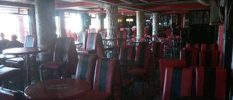 Um restaurante com cadeiras listradas em vermelho e preto, mesas redondas e teto alto com vigas aparentes.