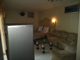 Quarto de hotel compacto com cama, sofá, mesa pequena e frigorífico.