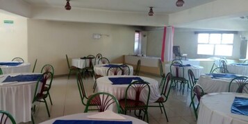 Quarto de hotel com várias mesas redondas e cadeiras verdes, disposto em um espaço amplo.