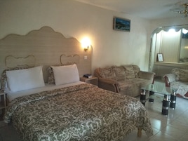 Quarto com cama grande, sofá, mesa de centro de vidro e espelho.