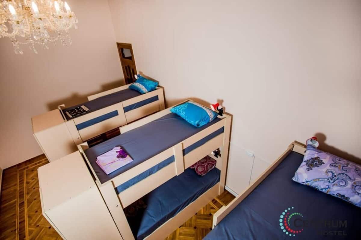 Quarto com beliche de madeira, duas almofadas, uma mesinha e um lustre.