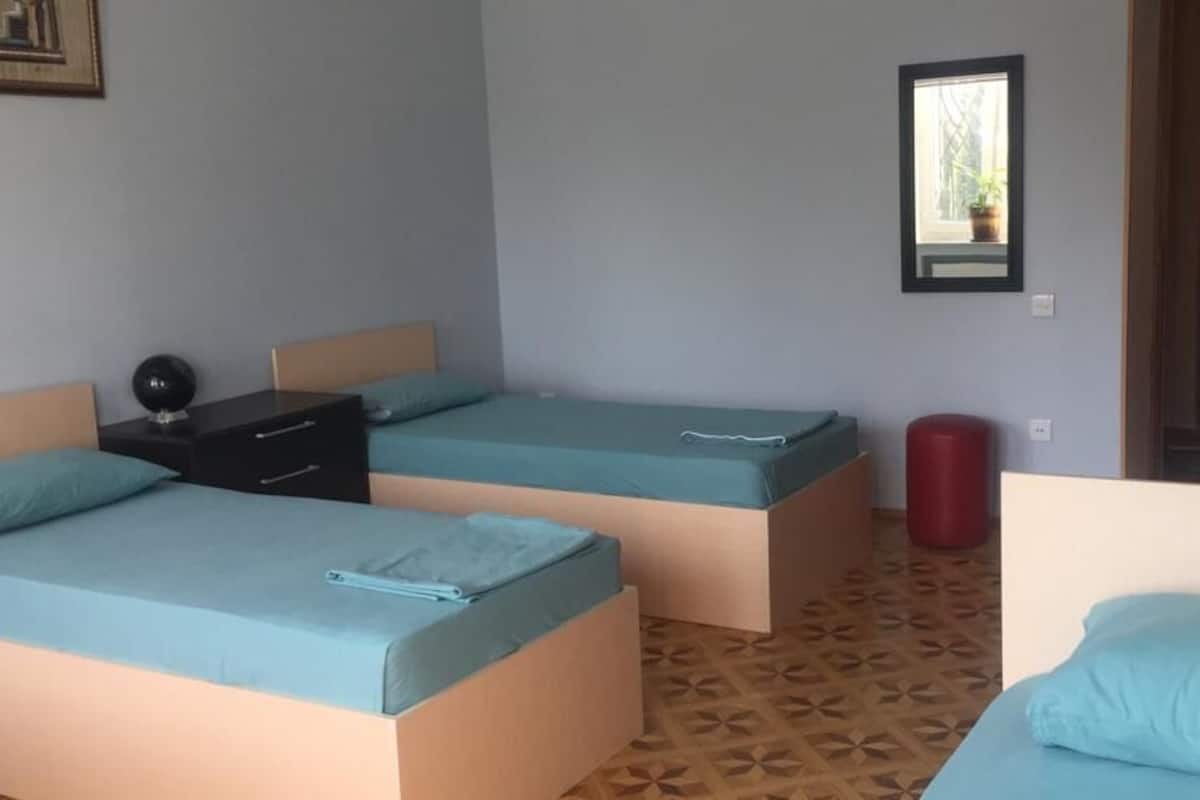 Quarto com duas camas, uma mesa pequena e uma lixeira vermelha.