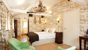 Quarto com cama, duas poltronas verdes, um lustre e parede com padrão de pedra.