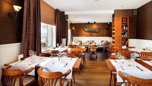 Um restaurante com várias mesas e cadeiras de madeira, uma parede decorativa com tema de dragão e uma estante com diversos objetos.