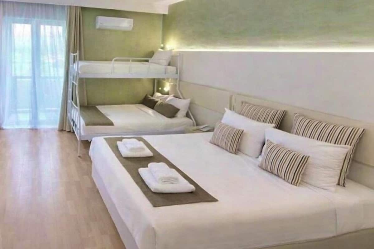 Quarto de hotel com uma cama grande, uma cama menor e uma cama beliche.
