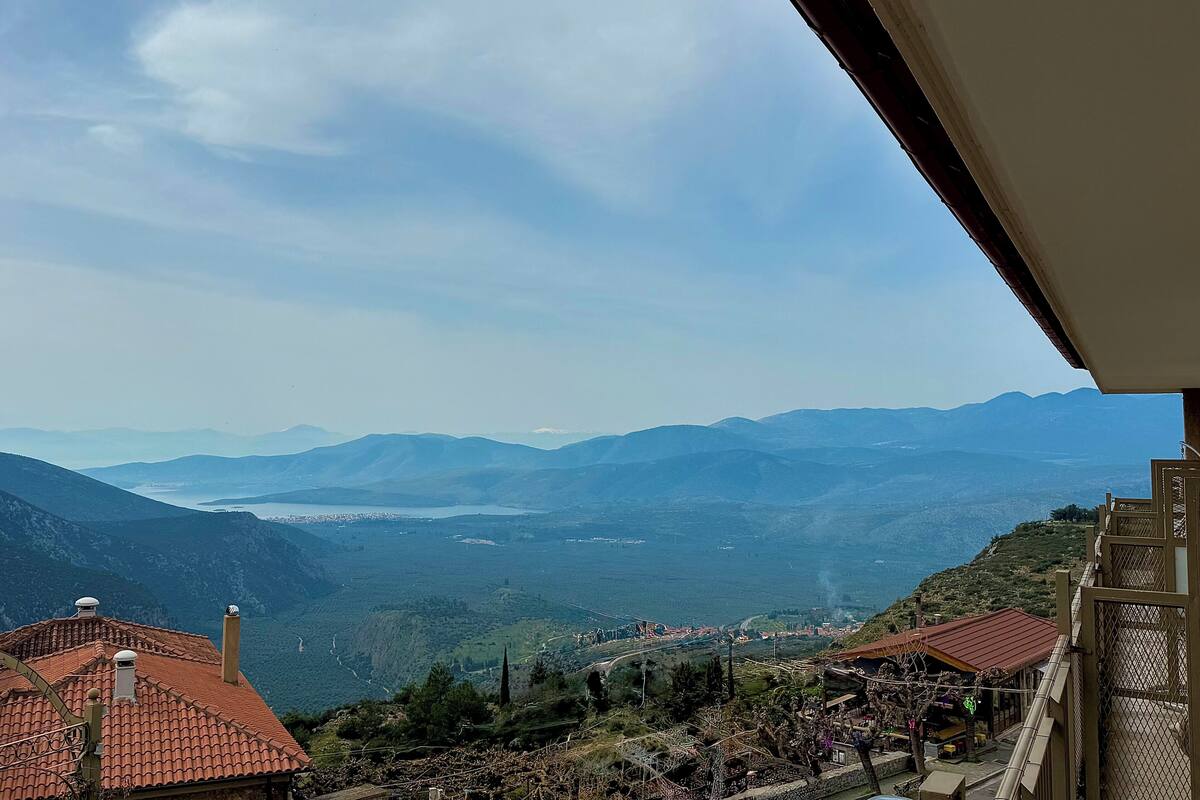 Vista de uma varanda com paisagem montanhosa, um lago e colinas ao longe.