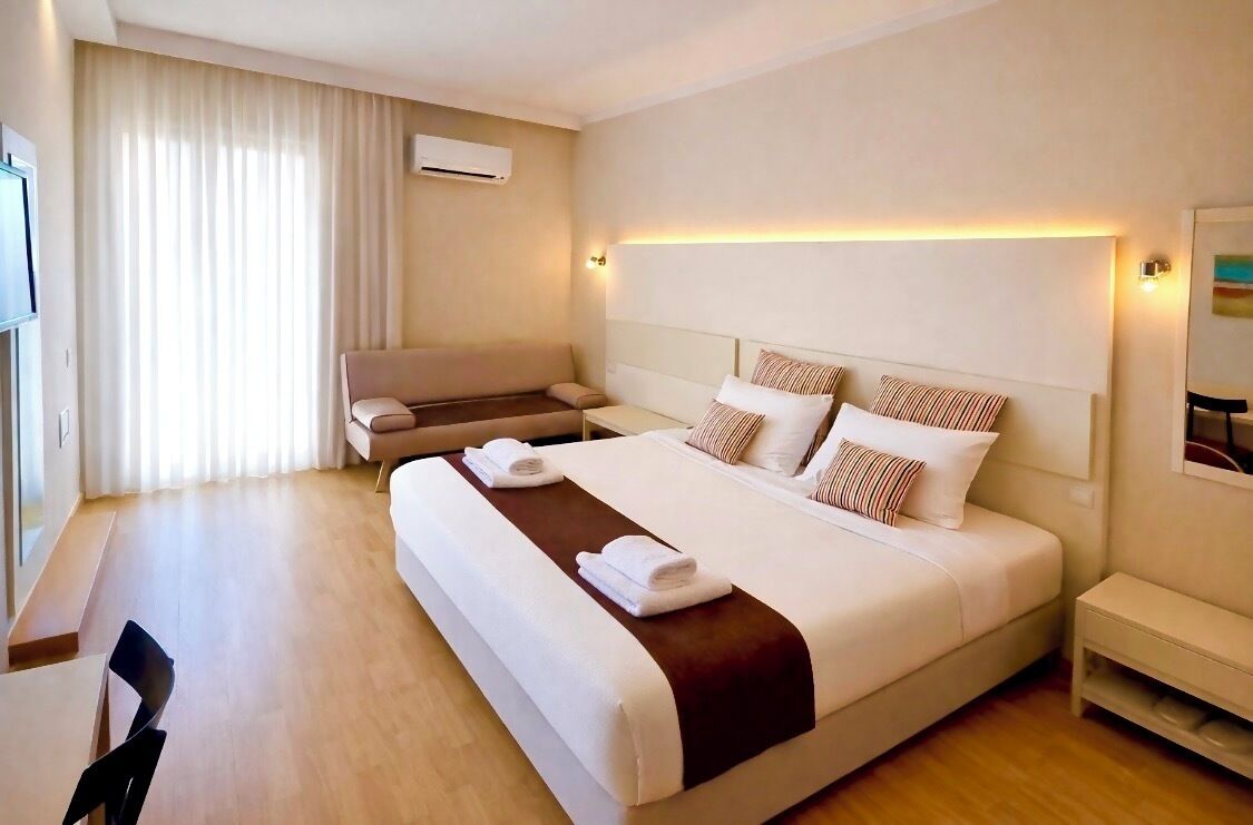 Quarto de hotel com uma cama grande, um sofá, uma escrivaninha e uma televisão.