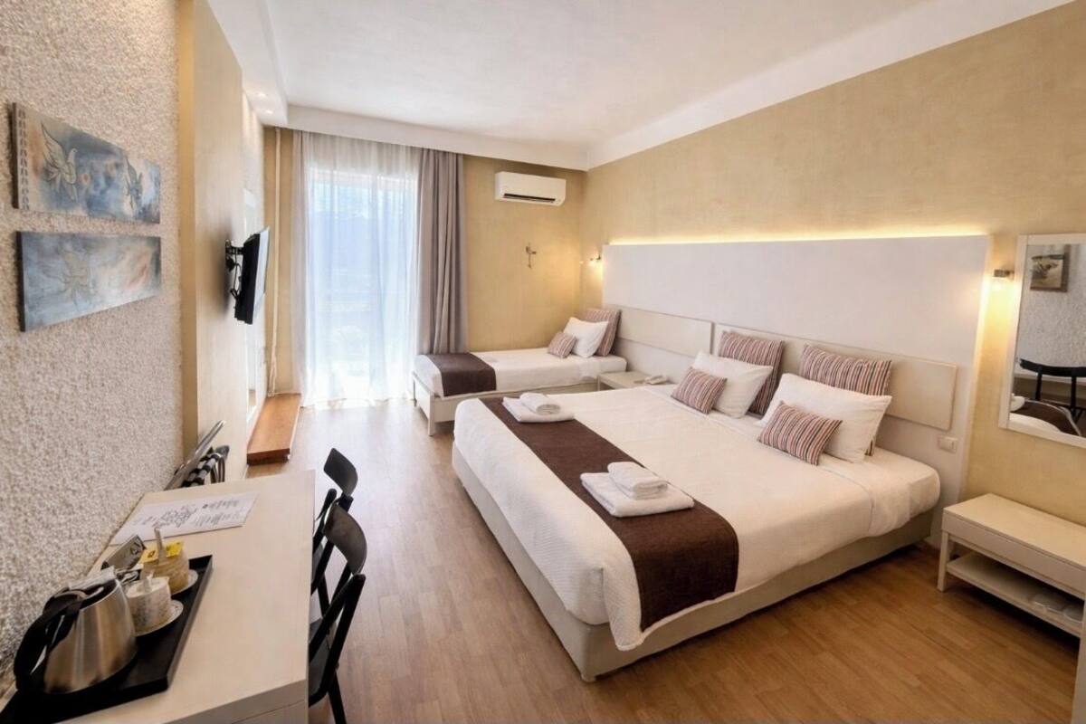 Quarto de hotel com duas camas, uma mesa de trabalho com cadeira, televisão e obras de arte nas paredes.