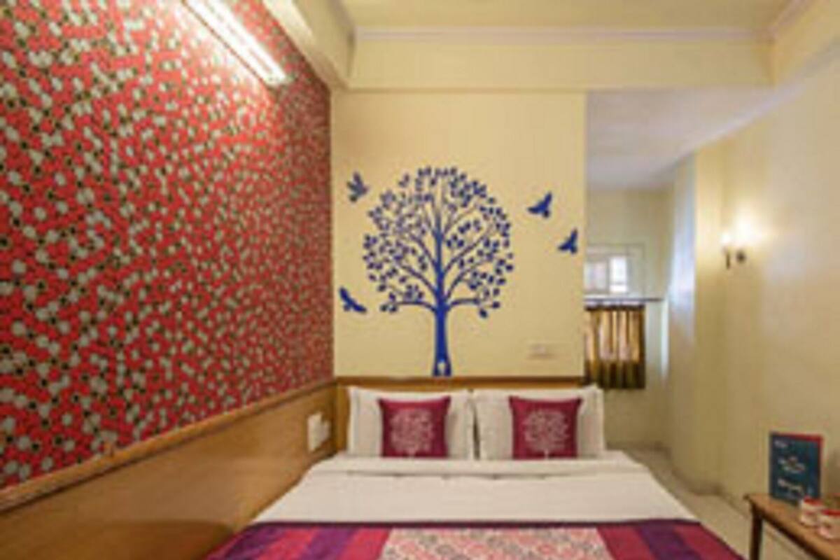 Quarto com cama, parede com árvore e pássaros, e uma parede estampada.