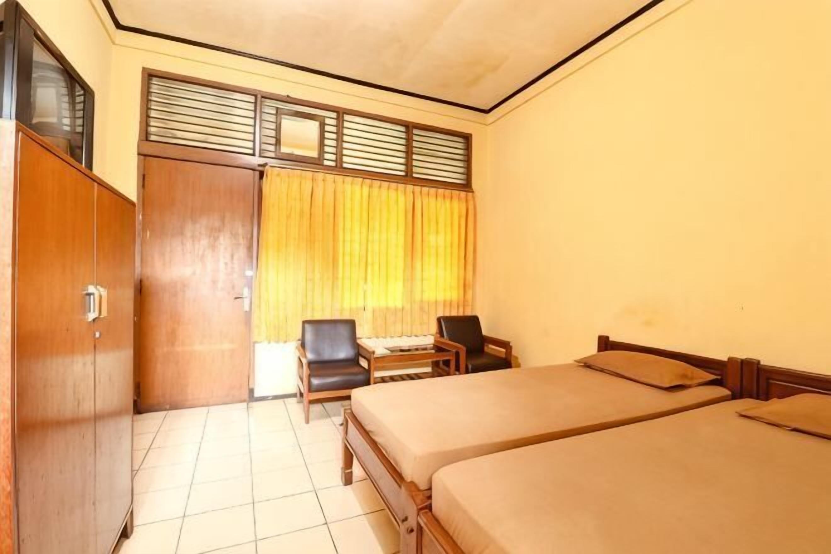 Quarto de hotel com duas camas, um guarda-roupa, uma secretária e uma cadeira.