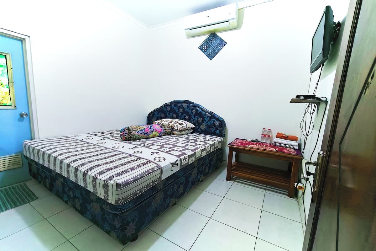 Quarto com uma cama, uma televisão, um aquecedor e uma pequena mesa com objetos em cima.