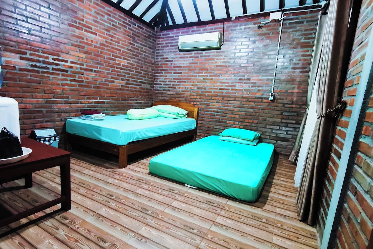 Quarto com duas camas, uma mesa e uma parede de tijolos.